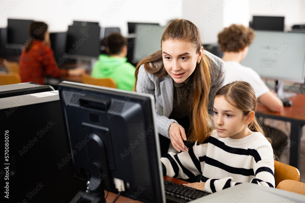 Female teacher and her student, young girl, looking at monitor of PC ...