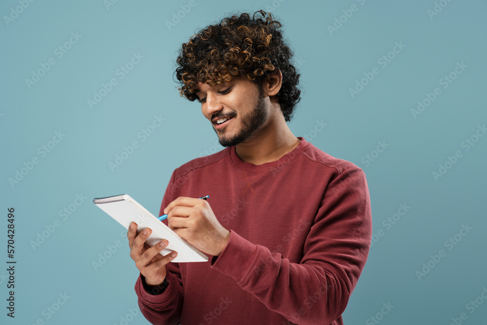Portrait of smiling Indian man taking notes in notepad isolated on blue ...