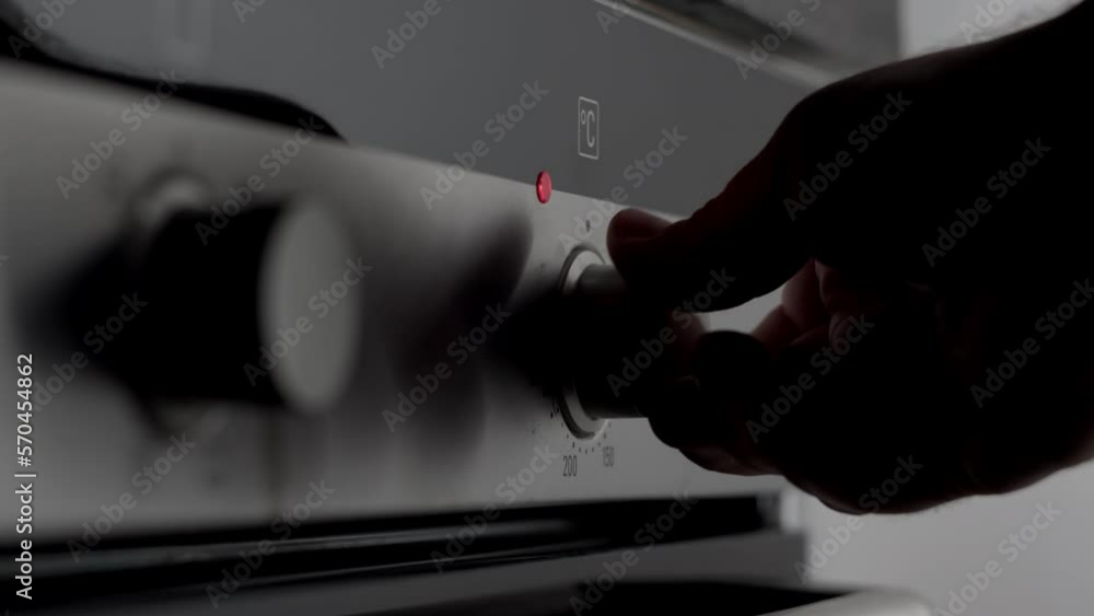 close up view of hand of person set temperature in oven. Turning on red ...