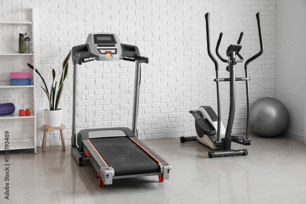 Interior of gym with modern treadmill and elliptical trainer near white ...