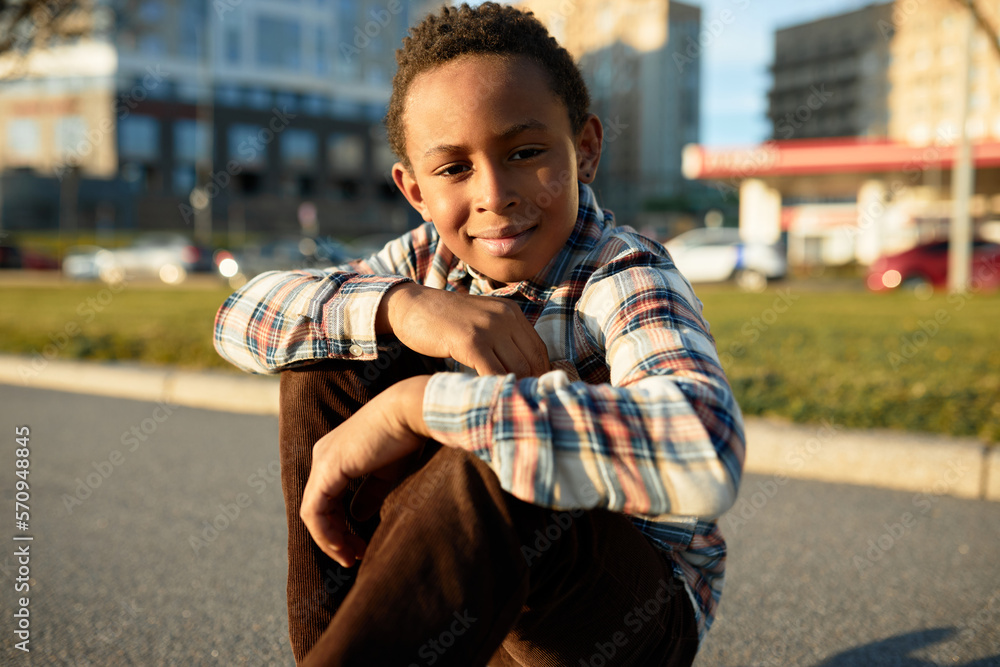 Handsome kid boy of african ethnicity sitting on pavement in brown ...