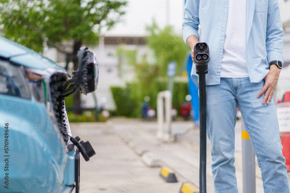 Handsome Asian young man holding an EV plug connector and attaching ...