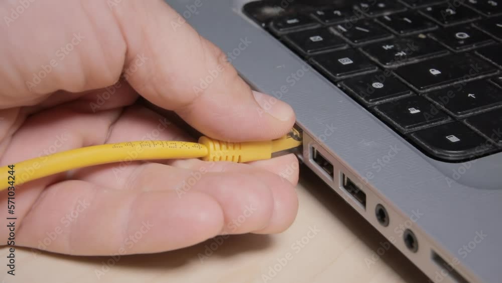A yellow ethernet cable wired to a laptop, and a hand removing and ...