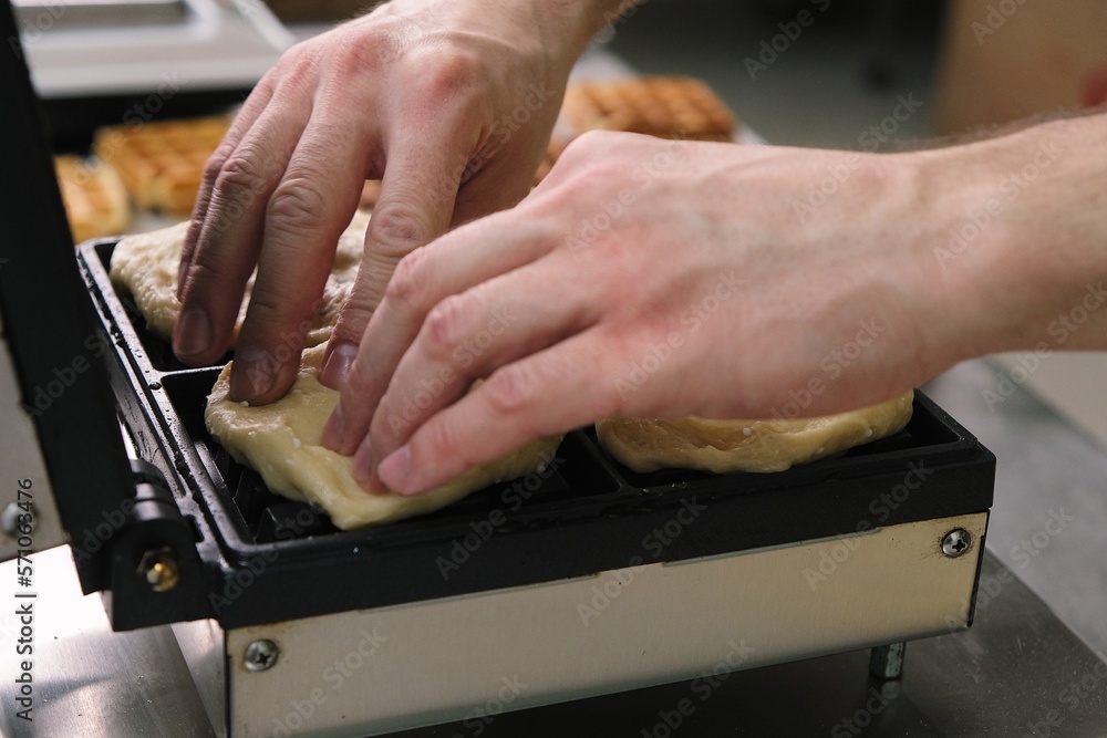 Close-up chef pours waffle batter in a waffle iron in a professional ...