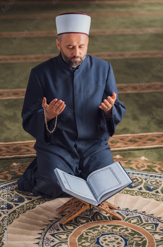 A Muslim prayer man praying with hands up while reading a Quran inside ...