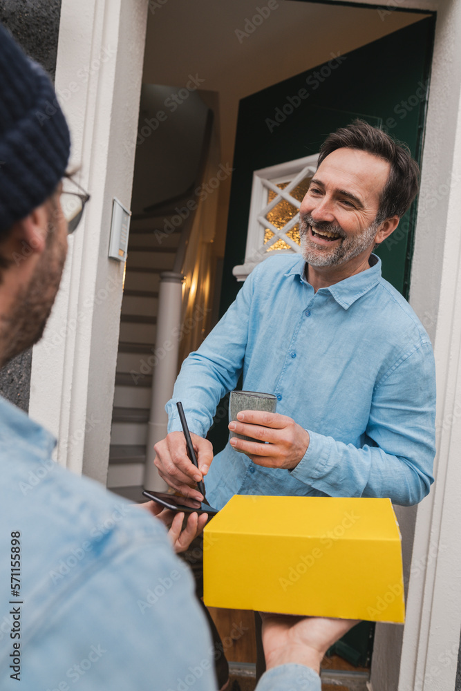 Happy customer signing and receiving package from delivery person at ...