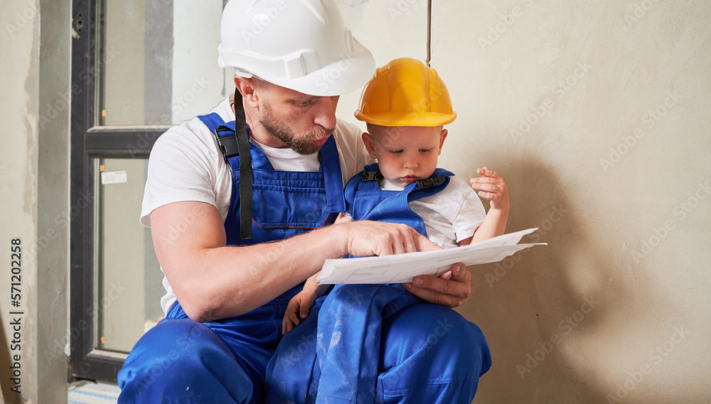 Male builder showing architectural drawings to little boy. Adorable ...