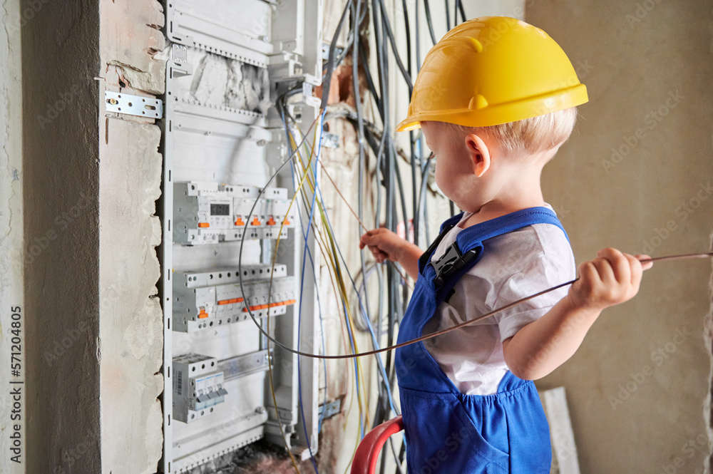 Little boy electrician in safety helmet holding electrical wires while ...