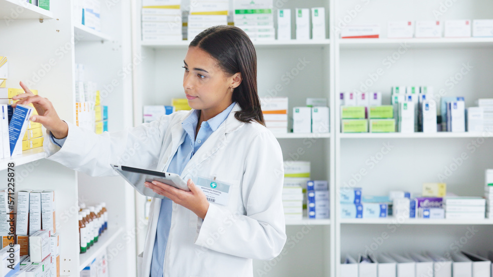 A young female pharmacist stocktaking in a dispensary using a tablet ...
