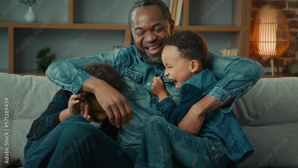 Affectionate African American family father dad tickling two little adorable children siblings ...