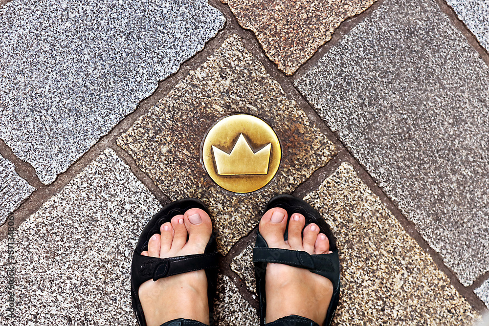 Top view of tired tourist legs in sandals and brass crown marker in ...