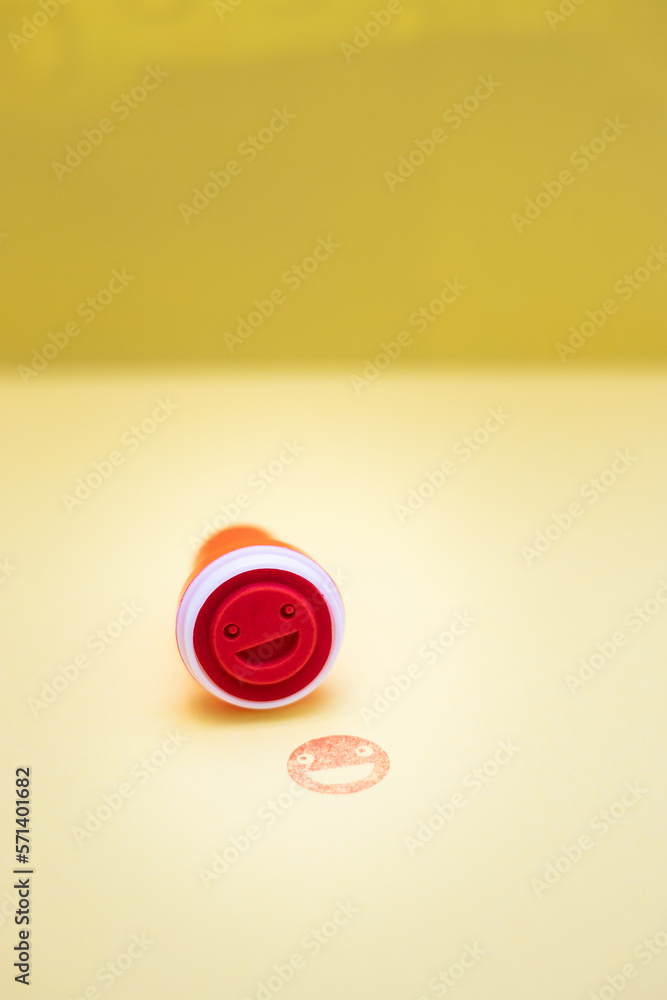 A stamp in the shape of a smiling face, is upside down on a yellow ...