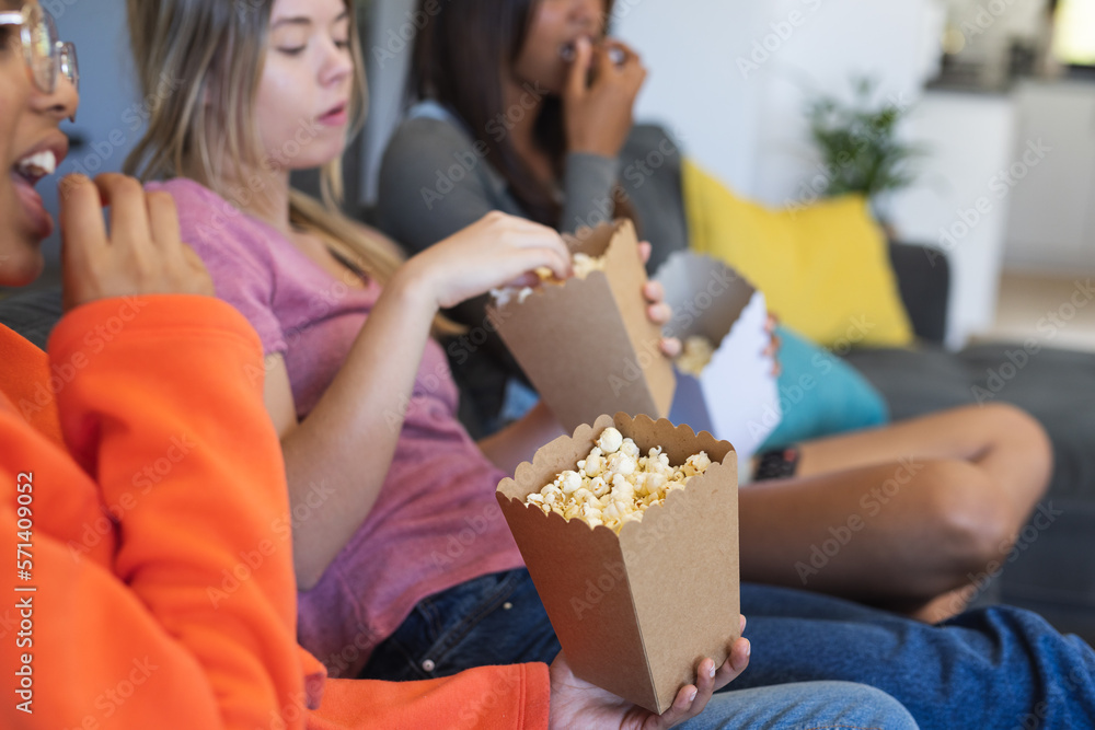 Happy diverse teenage female friends eating popcorn and watching tv ...