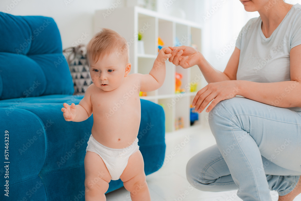 Cute little baby in a diaper learning to walk in a white room , mom ...