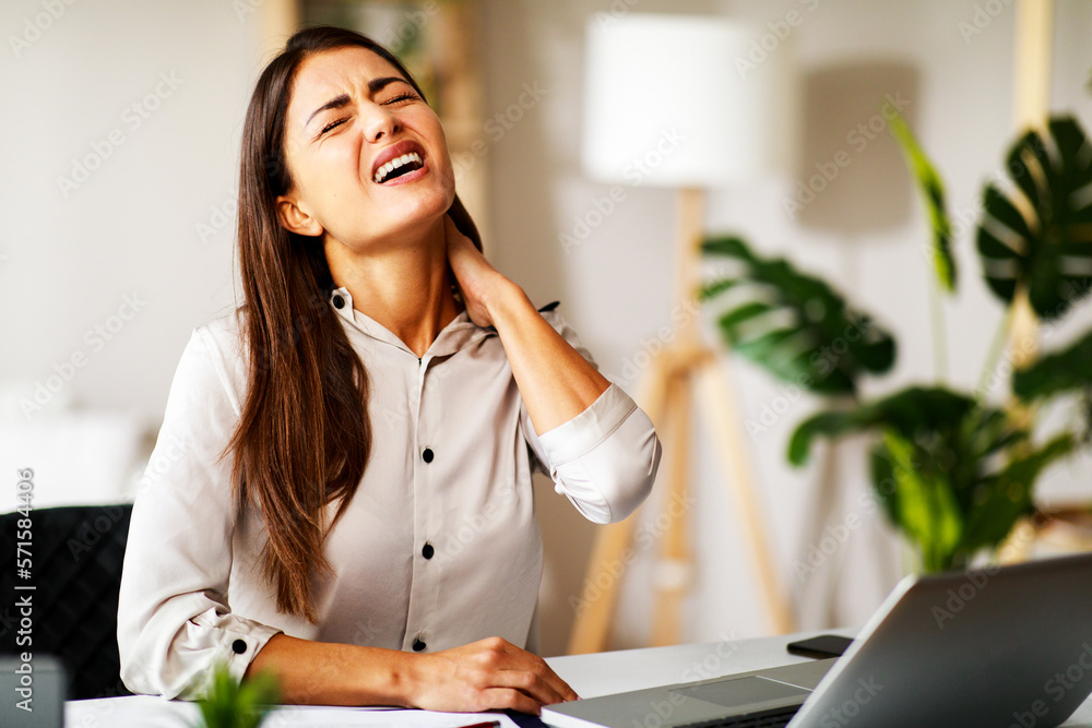 Young woman is sitting at a desk in the office and has neck pain while ...