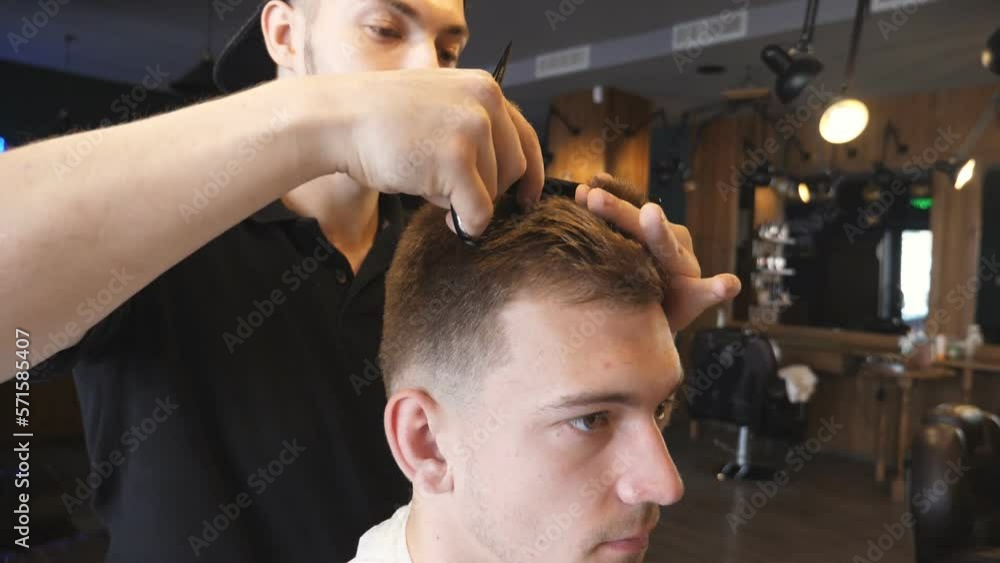 Close up of male barber combing and cutting hair of his young customer ...