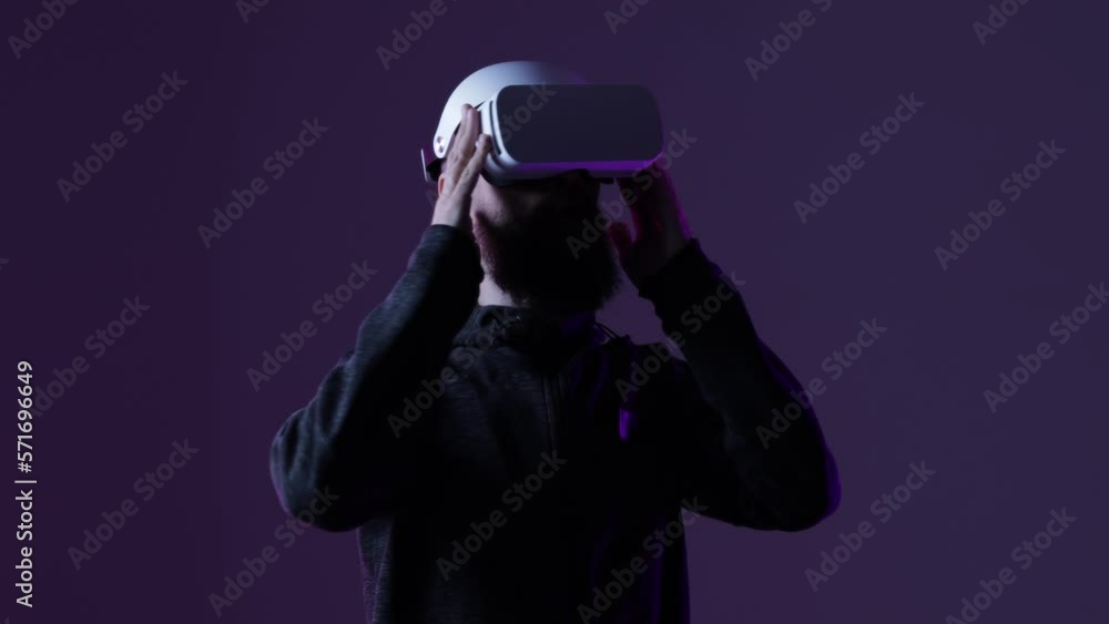 Young man in futuristic costume on dark background. Guy using VR helmet ...