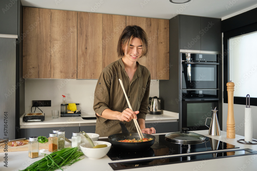 Smiling asian young man cooking chinese or taiwanese tomato scrambled ...