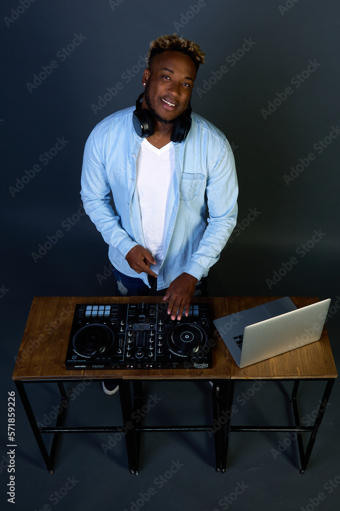Black man stands behind a DJ station in jeans and a loose shirt turns ...