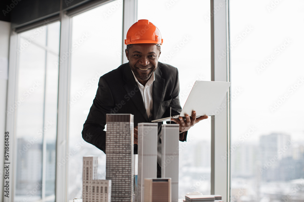 Focused african inspector using laptop inspecting skyscraper model in ...