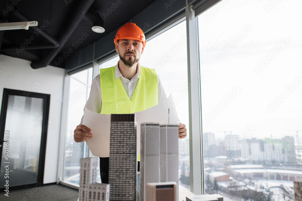Young builder in hard hat holding blueprint working on building complex ...