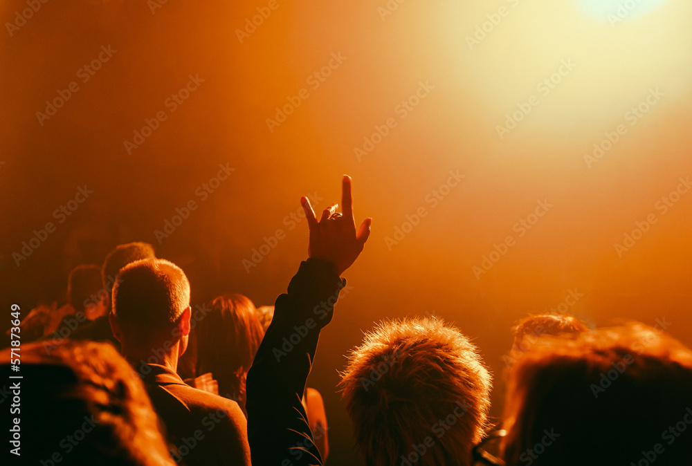 Man in crowd raising hand with devil horns in orange spotlight at a ...