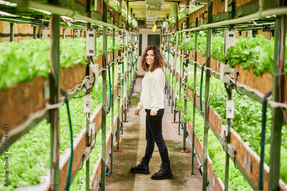 Portrait of female person looking at green leafy plants in greenhouse ...