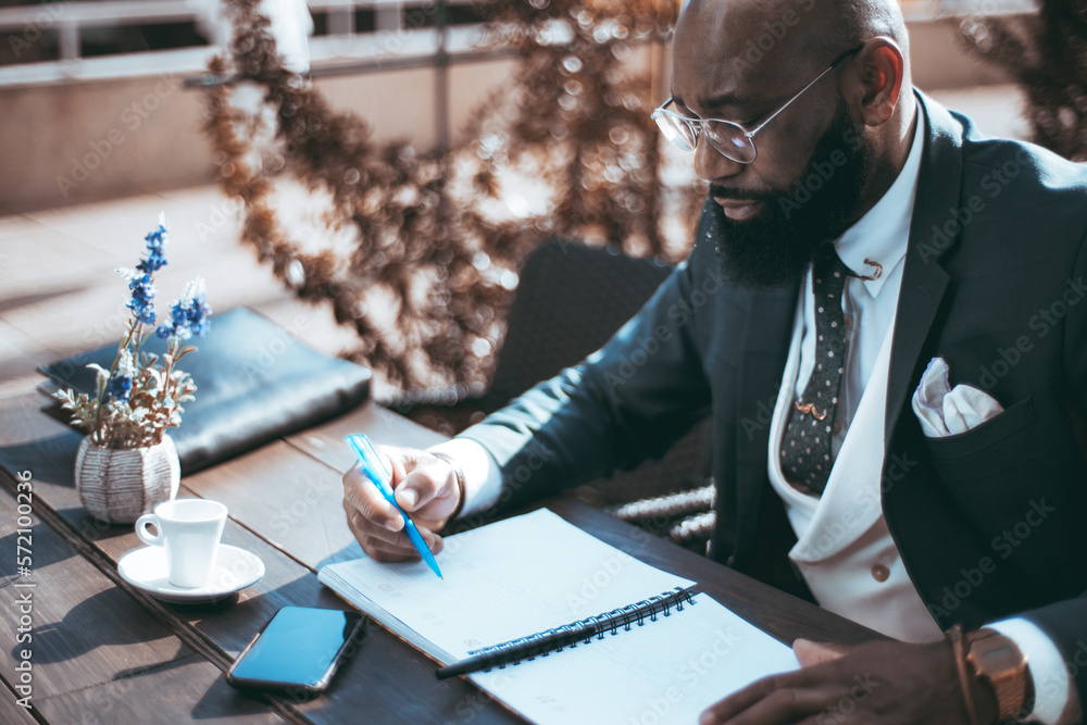 An African writer with a full-grown beard sitting on an outdoor ...