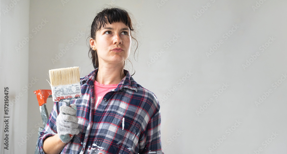 puzzled woman in paint roller and white paint for walls in hands close ...