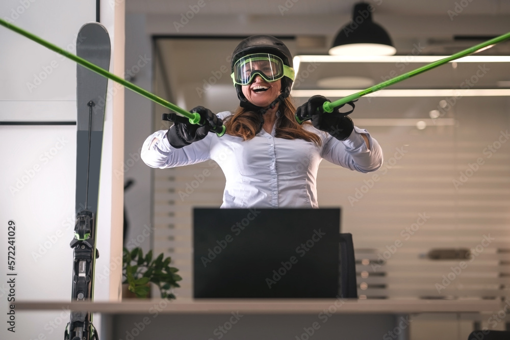 Woman in an office with ski helmet and ski goggles on the head holds ...