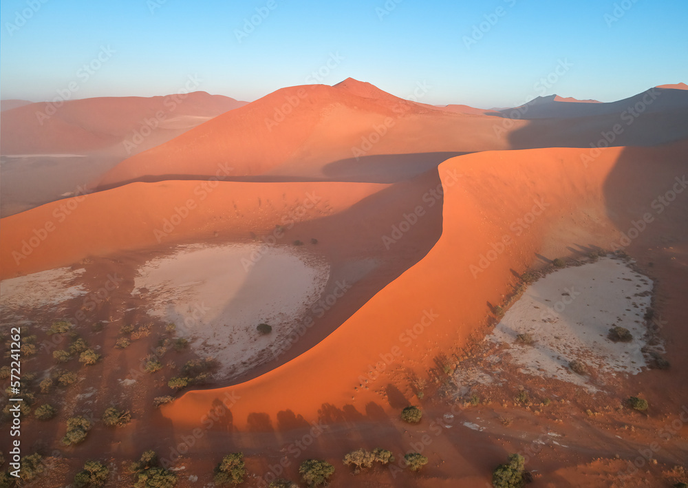 Shapes and shadows of vast orange sand dunes, illuminated by rising sun ...