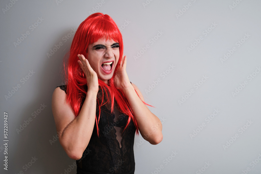 Portrait of drag queen screaming and wearing a red wig on grey ...