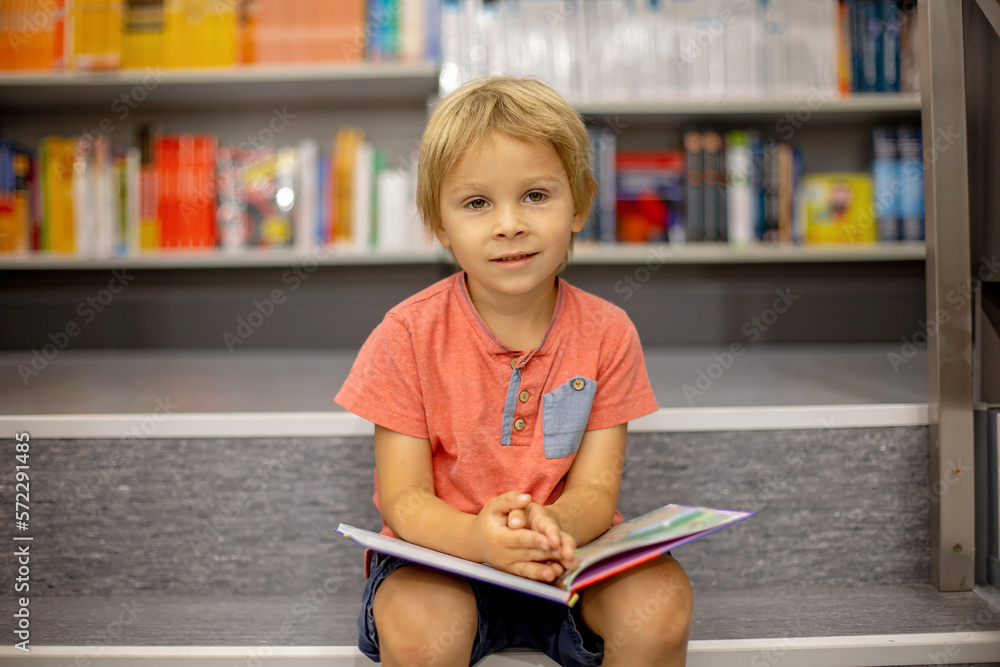 Cute preschool child, looking at books in a bookstore on summer day ...
