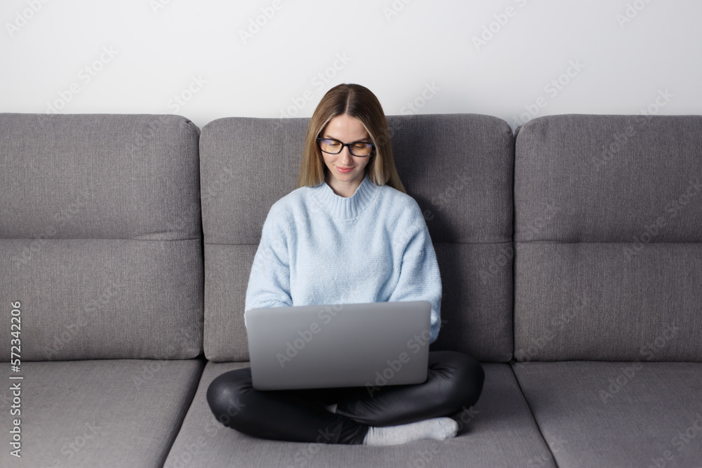 Foto de Beautiful blonde woman sitting on couch and working on silver ...