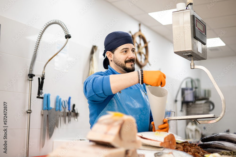 A middle-aged fishmonger in an apron and a hat is filling a paper ...