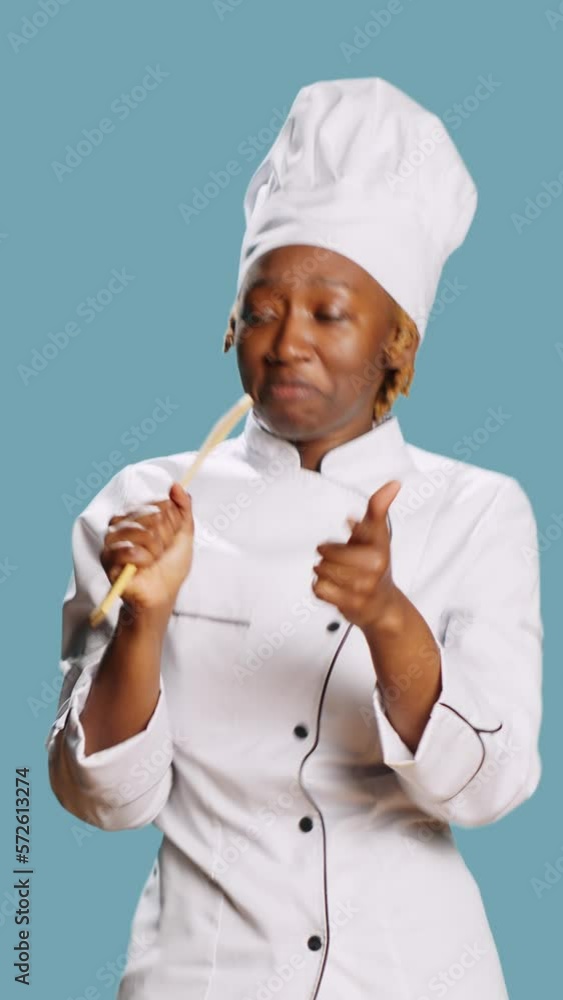 Vertical video: Young happy chef using wooden spoon to sing in studio ...