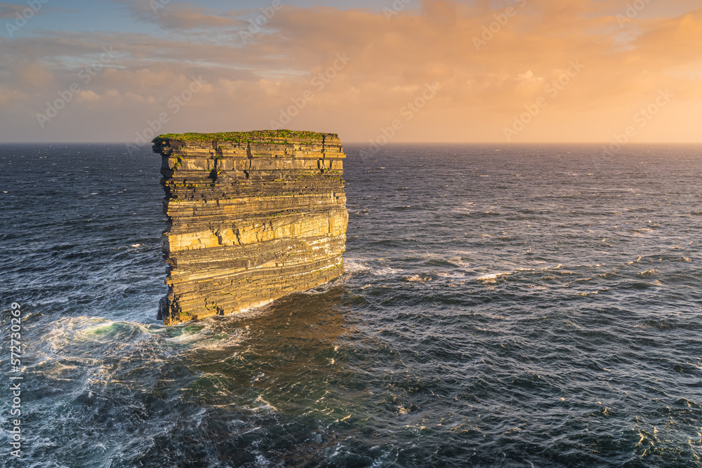 Downpatrick Head sea stack illuminated by sunrise, with rock layers of ...
