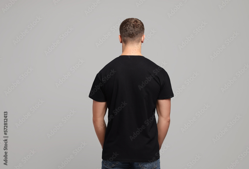 Man wearing black t-shirt on light grey background, back view. Mockup ...