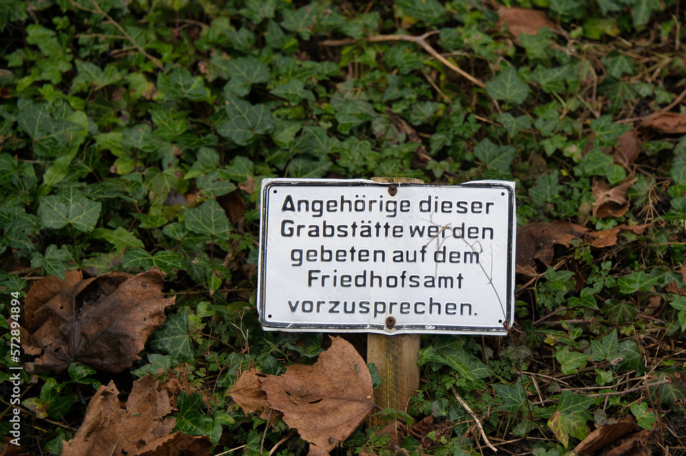 Hinweisschild mit der Bitte sich zu melden auf einem Friedhof in ...