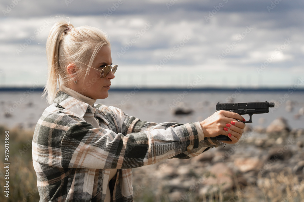 Beautiful girl in sunglasses by the sea with a 9mm pistol in her hands ...