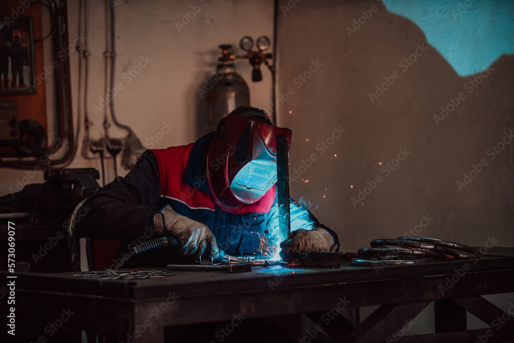 Profesional welder in protective uniform and mask welding metal pipe on ...