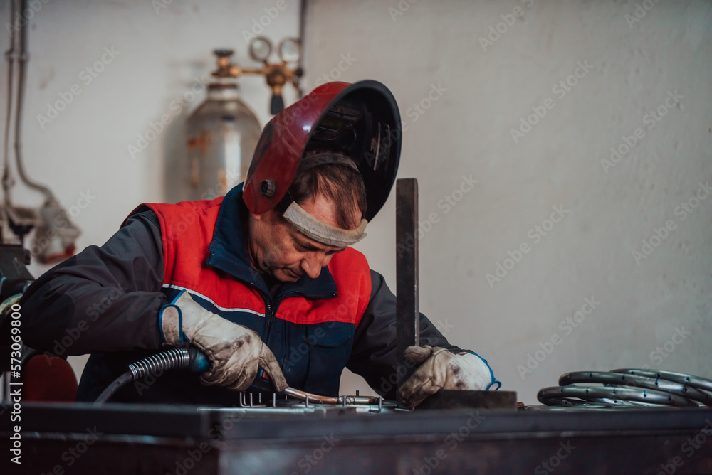 Profesional welder in protective uniform and mask welding metal pipe on ...