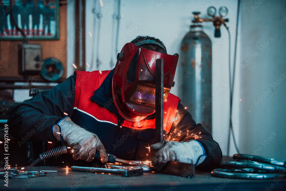 Profesional welder in protective uniform and mask welding metal pipe on ...