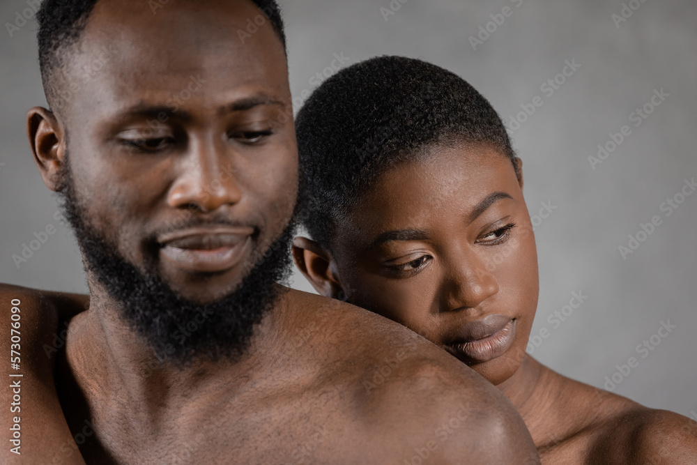 Serious Black woman embracing Black shirtless boyfriend looking down ...