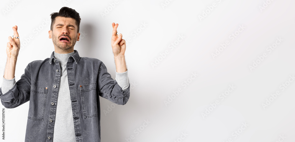 Sad and miserable man hoping god, cross fingers and crying, praying or ...