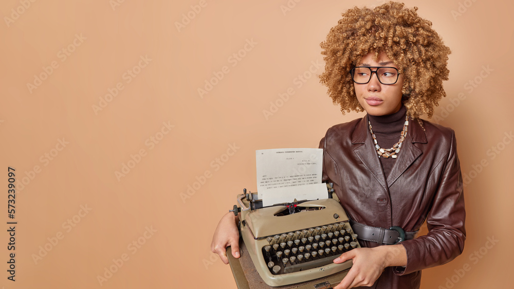 Studio shot of curly haired female secretary types retro typewriter ...