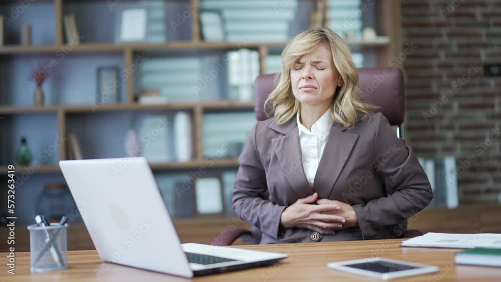 Sick mature businesswoman is feeling abdominal pain at the desk at the ...