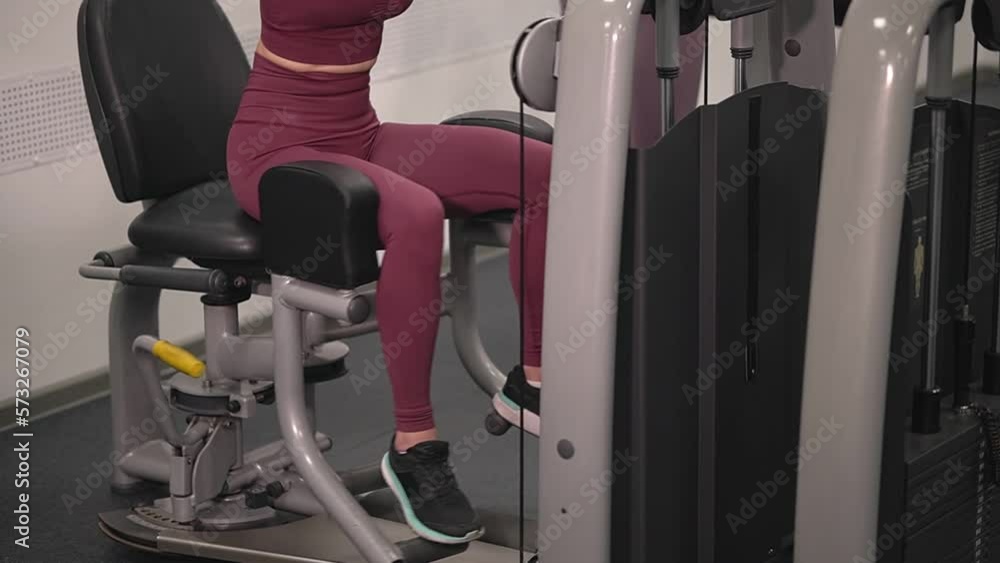 the girl is engaged in the simulator. she does exercises on leg muscles ...