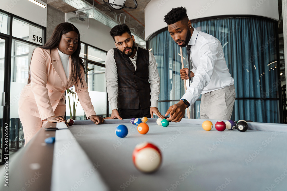 Young multiracial people in suits playing pool at office lobby Stock ...