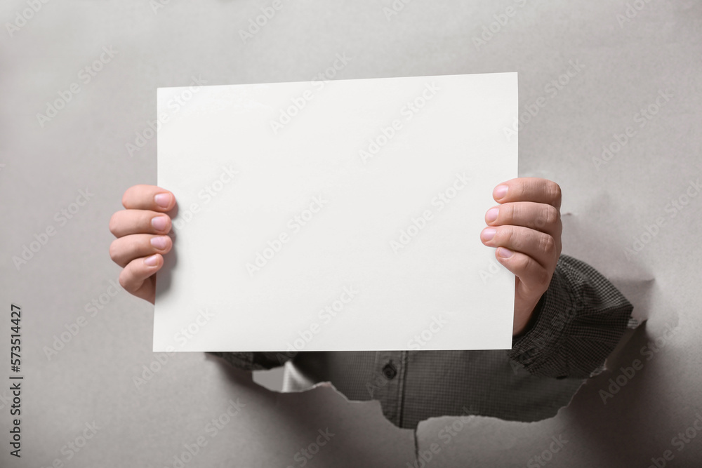 Man holding sheet of paper through hole in white paper, closeup. Mockup ...